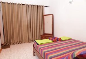 Quarto com cama, mesa de cabeceira de madeira, espelho e cortinas bege.