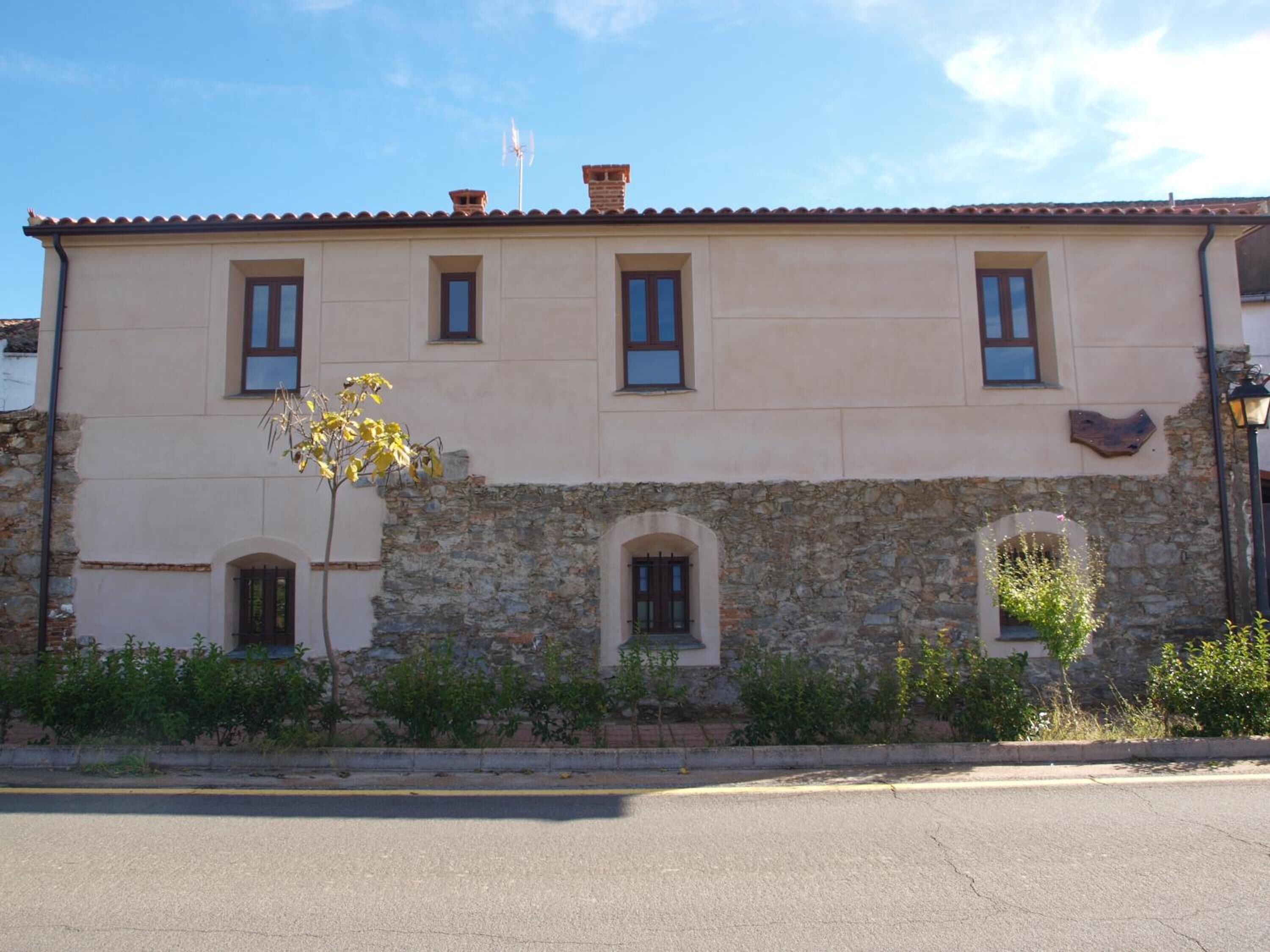 Um edifício de dois andares com fachada de pedra, várias janelas e um pequeno jardim na frente.
