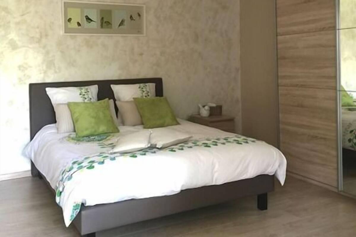 Quarto moderno com cama, almofadas, mesa de cabeceira e um quadro de pássaros na parede.