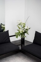 Um espaço de estar no canto com cadeiras estofadas pretas e um vaso preto com flores brancas.