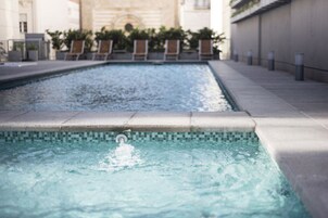 Piscina com borda azulejada, rodeada por espreguiçadeiras e um muro baixo.