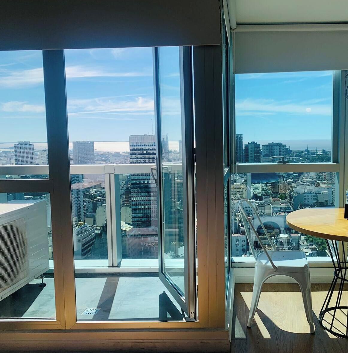 Um apartamento alto com uma grande janela de vidro, uma cadeira branca e uma mesa redonda.