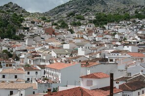 Uma cidade densamente povoada com edifícios brancos e telhados de telha vermelha, rodeada por colinas rochosas e vegetação.
