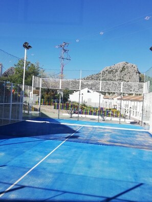Uma quadra esportiva com rede, cercada por uma grade, e uma montanha ao fundo.