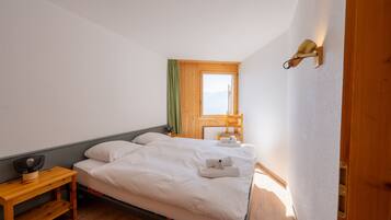 Quarto com cama, mesa de cabeceira, janela com cortinas e luminária na parede.
