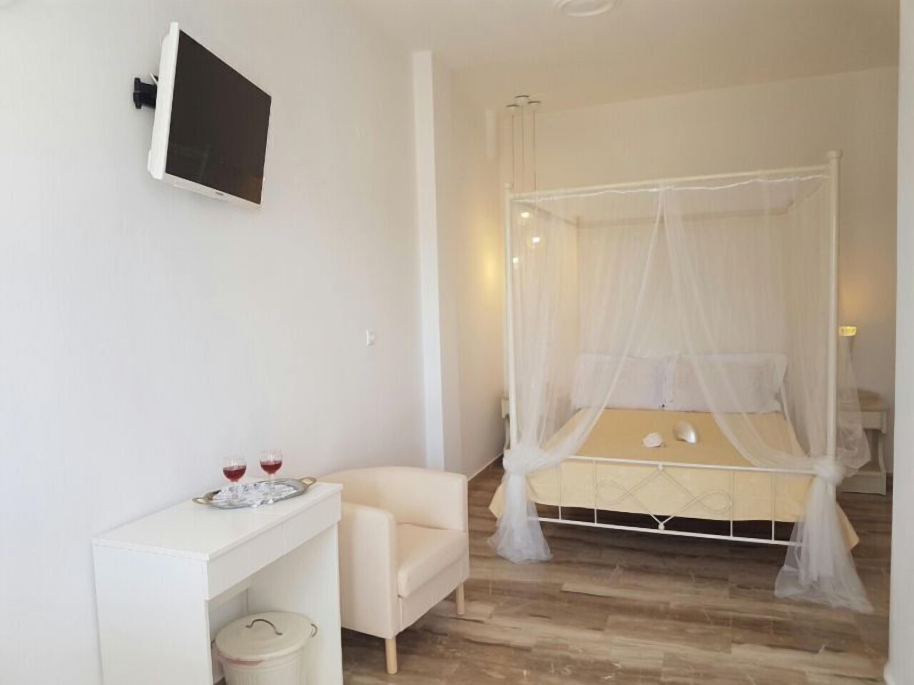 Quarto com cama de dossel, uma escrivaninha branca com um jogo de copos e uma cadeira branca.