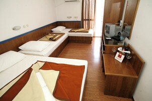 Quarto de hotel com duas camas, uma televisão, uma mesinha com uma garrafa e copos, e um espelho.