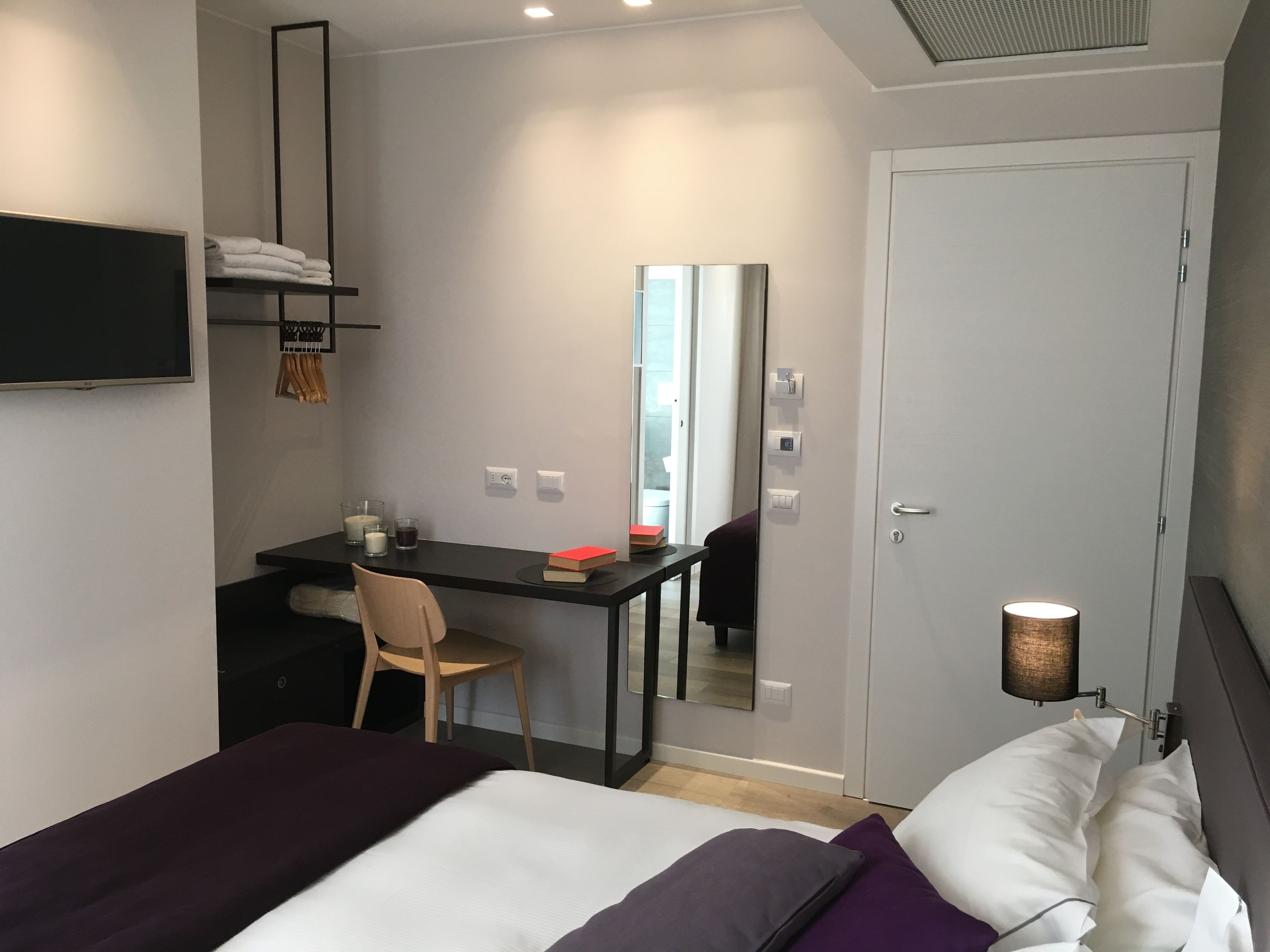 Quarto de hotel moderno com cama, escrivaninha, cadeira, espelho e abajur.