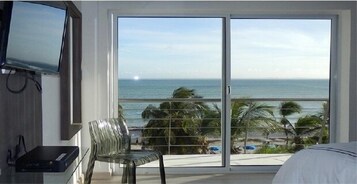 Quarto com uma grande porta de correr de vidro que dá para uma varanda com vista para o oceano e palmeiras.