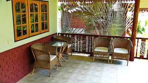 Um alpendre coberto com móveis de vime, piso de azulejos e vista através de um biombô de bambu.