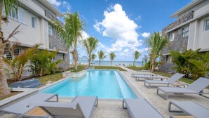 Uma área de piscina com espreguiçadeiras, palmeiras e vista para o mar.