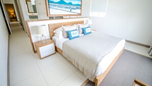 Quarto de hotel com uma cama grande, uma mesa de cabeceira com abajur, uma TV acima da cama e um banheiro com espelho e pia.