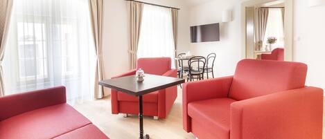Quarto de hotel moderno com um sofá vermelho, uma mesa pequena e uma televisão fixada na parede.