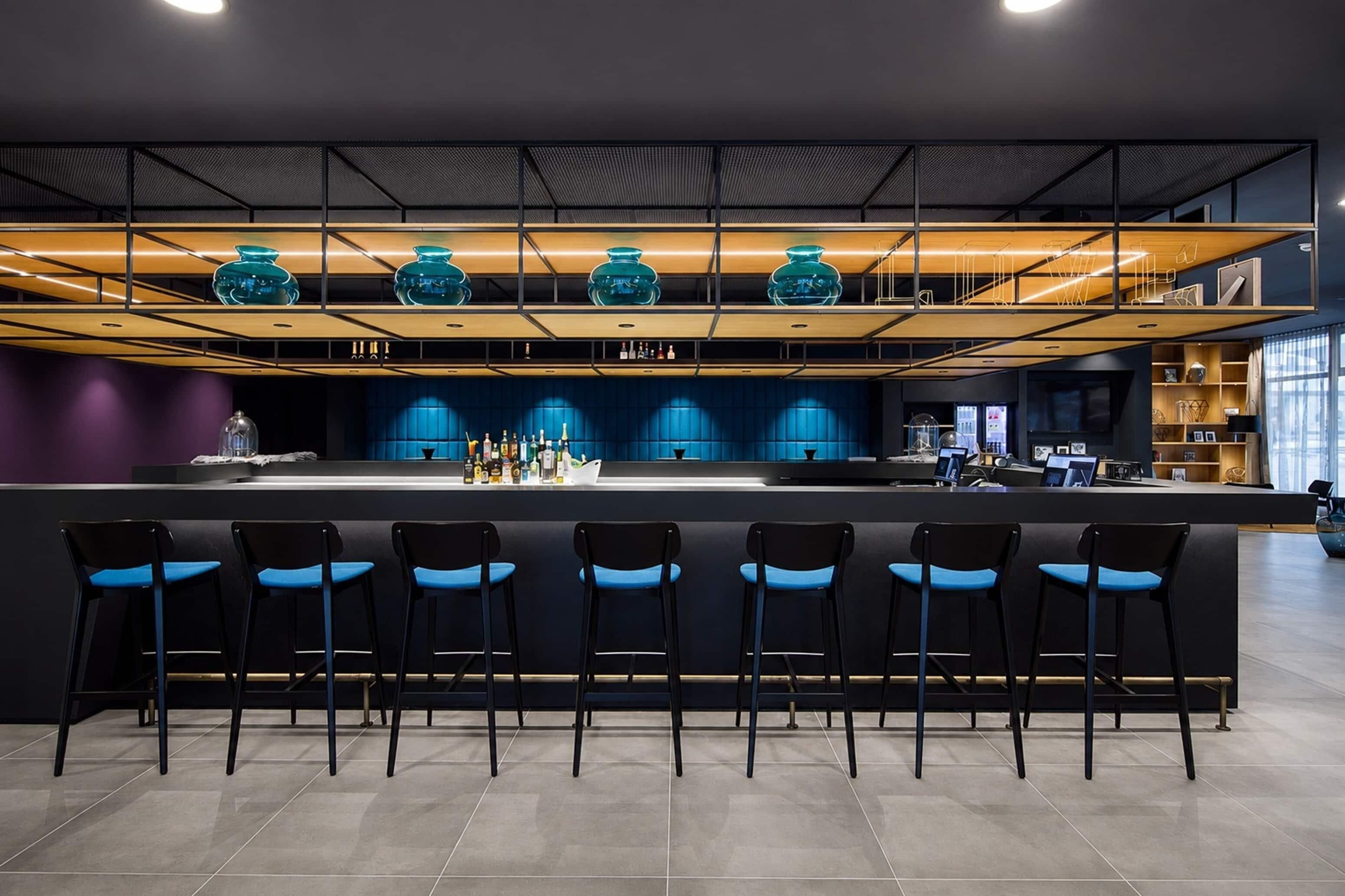 Uma área de bar com balcão, banquetas e iluminação azul no teto.