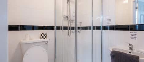 Casa de banho moderna com chuveiro envidraçado, sanita branca e lavatório com uma toalha pendurada na parede.