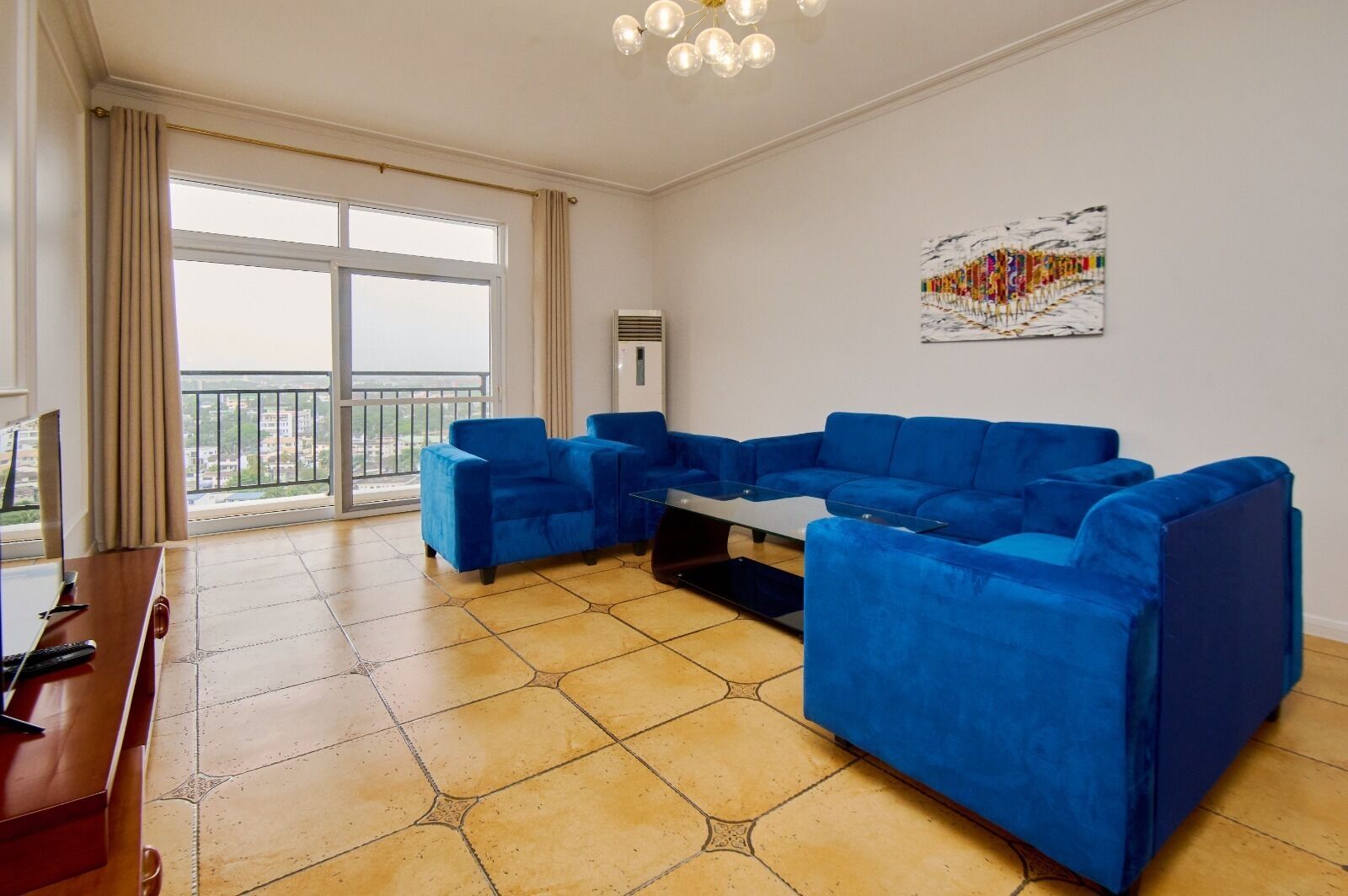 Sala de estar com sofá azul em forma de L, mesa de centro de madeira e uma janela grande com vista para edifícios.