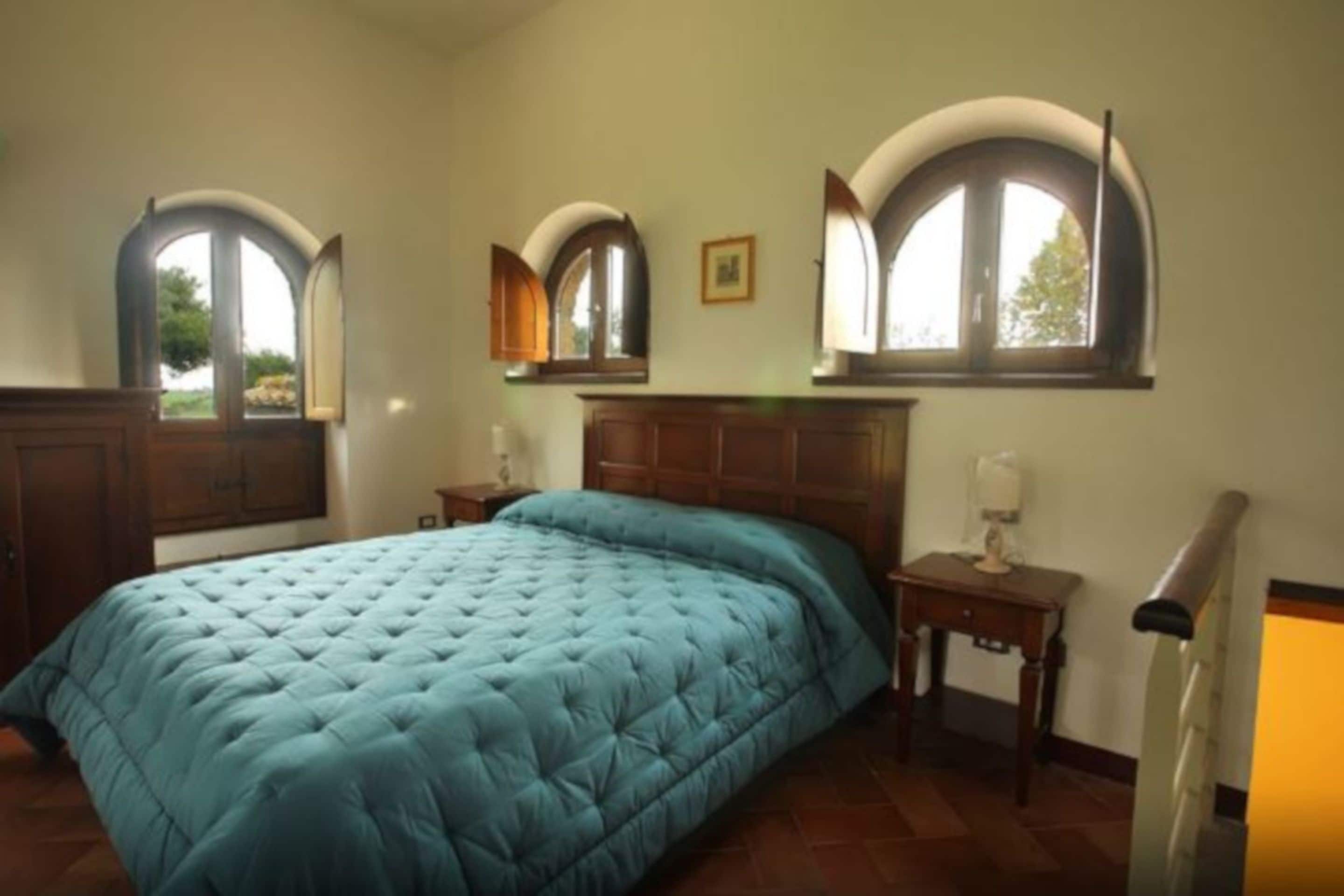 Quarto com cama grande, duas mesinhas de cabeceira, um criado-mudo e janela com design em arco.