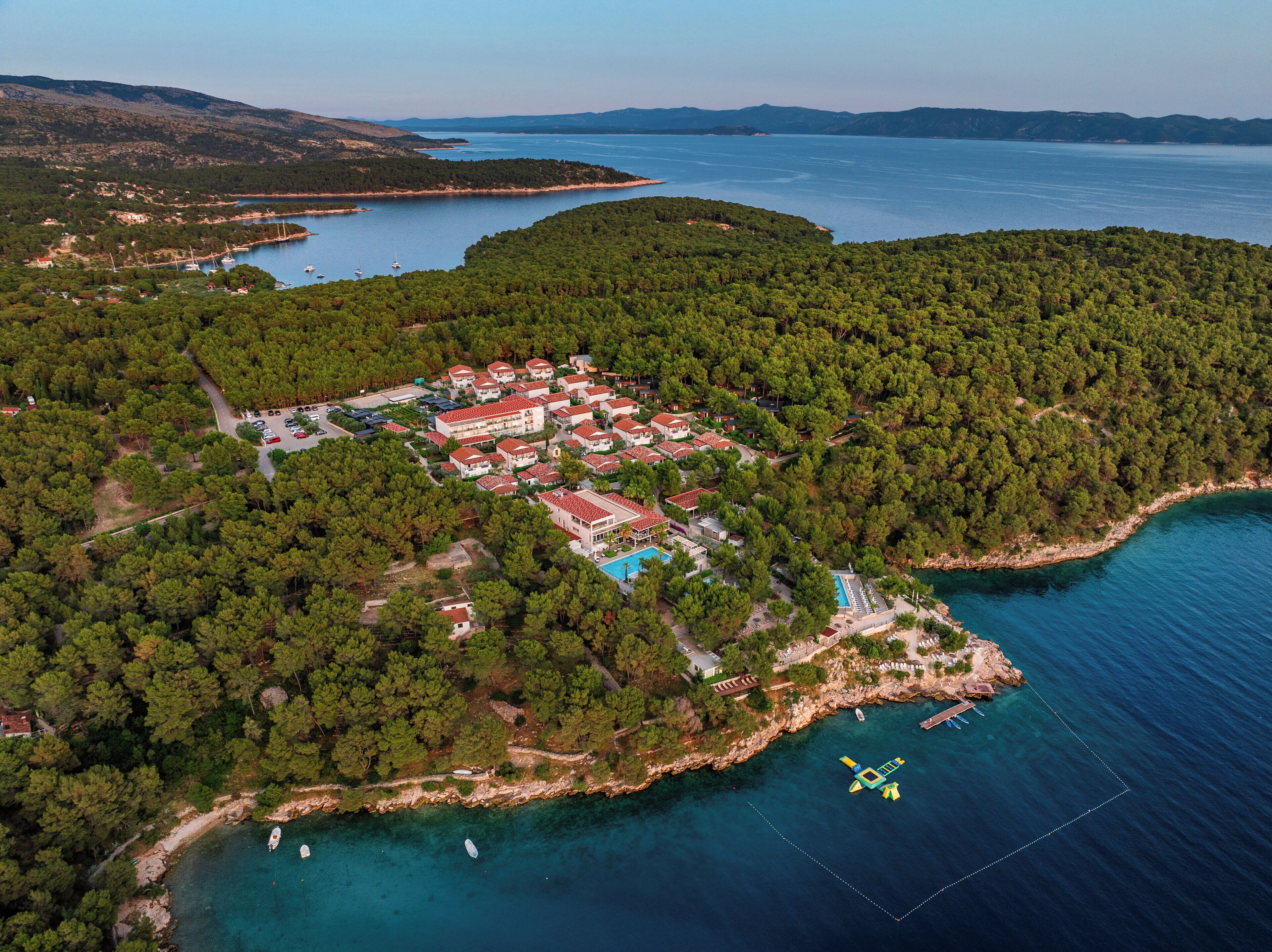 Vista aérea de um resort costeiro com vários edifícios, uma piscina e barcos na água.