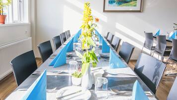 Uma sala de conferências com uma mesa comprida preparada para uma reunião, cadeiras dispostas ao redor e um quadro com uma paisagem na parede.