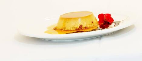 Uma porção de flan num prato branco com um toque de decoração vermelha.