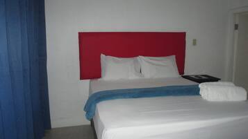 Quarto de hotel com cama, cabeceira vermelha, roupa de cama branca e cortina azul.