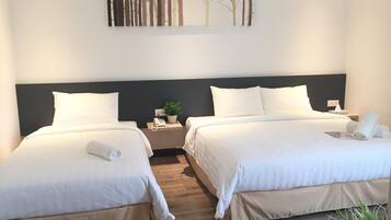 Quarto de hotel com duas camas, cabeceira escura, obra de arte pendurada na parede, mesas de cabeceira com luminárias e uma pequena planta em vaso.
