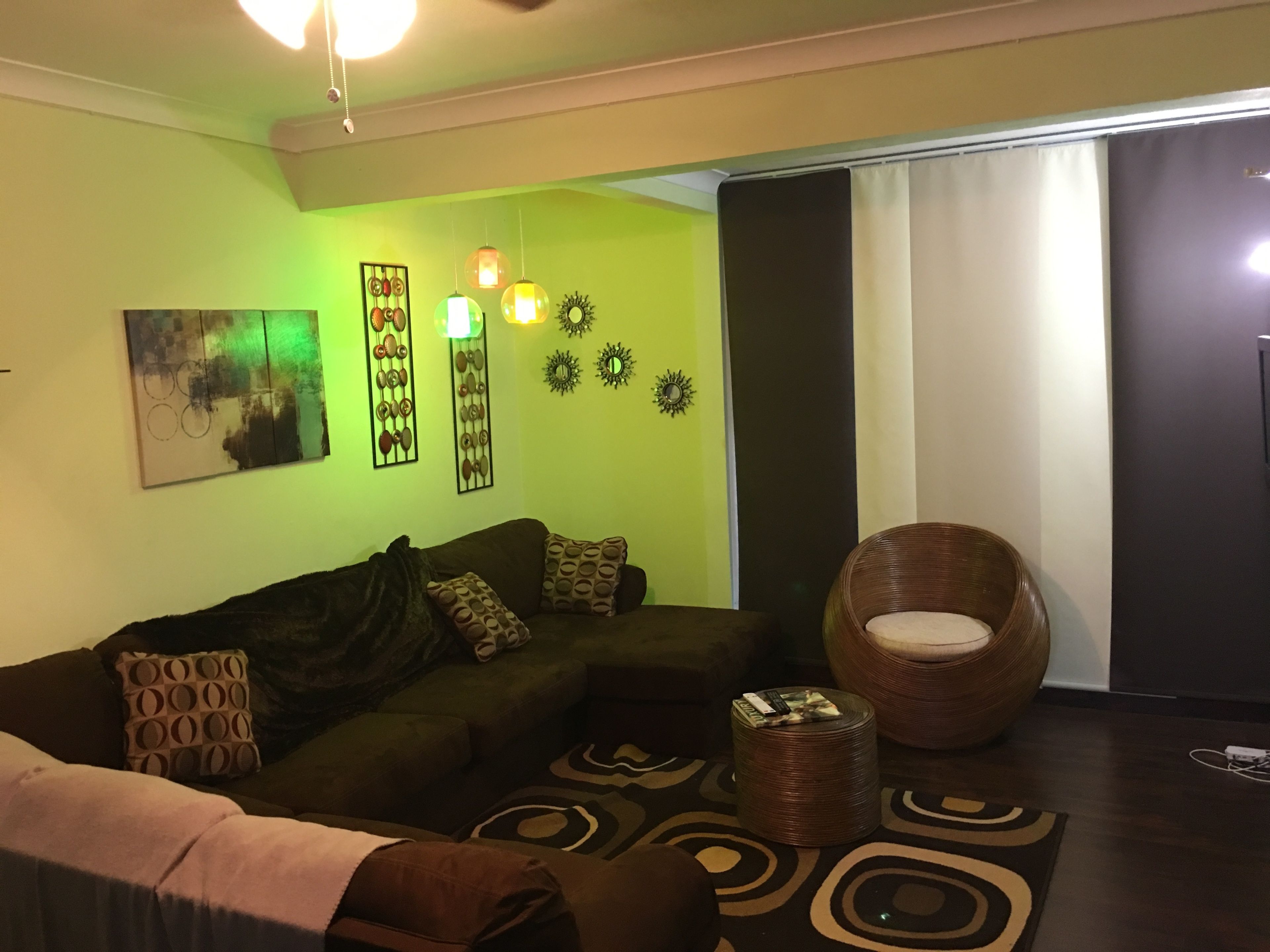 Sala de estar com parede verde, sofá marrom, cadeira de vime e tapete estampado.