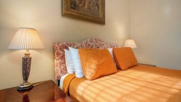 Cama bem arrumada com cabeceira estampada, duas luminárias laterais e um quadro na parede.