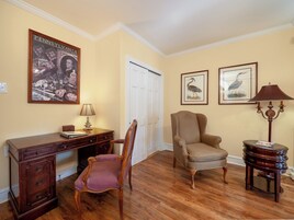 Quarto com escrivaninha de madeira, cadeira, luminária e duas molduras na parede.