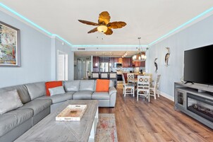 Uma sala de estar moderna com um sofá cinzento, uma mesa de centro de madeira e uma televisão sobre um suporte.