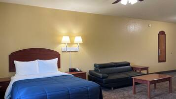 Quarto de hotel com cama, escrivaninha, cadeira, mesa de cabeceira, luminária, ventilador de teto e relógio de parede.