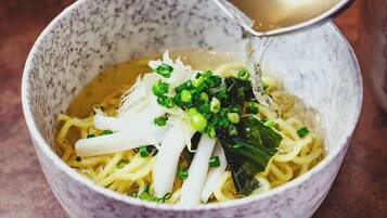 Uma tigela de ramen com macarrão, cebolinha e alga marinha sendo adicionada.