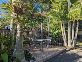 Uma área de pátio com mesa e cadeiras, cercada por palmeiras e plantas tropicais.