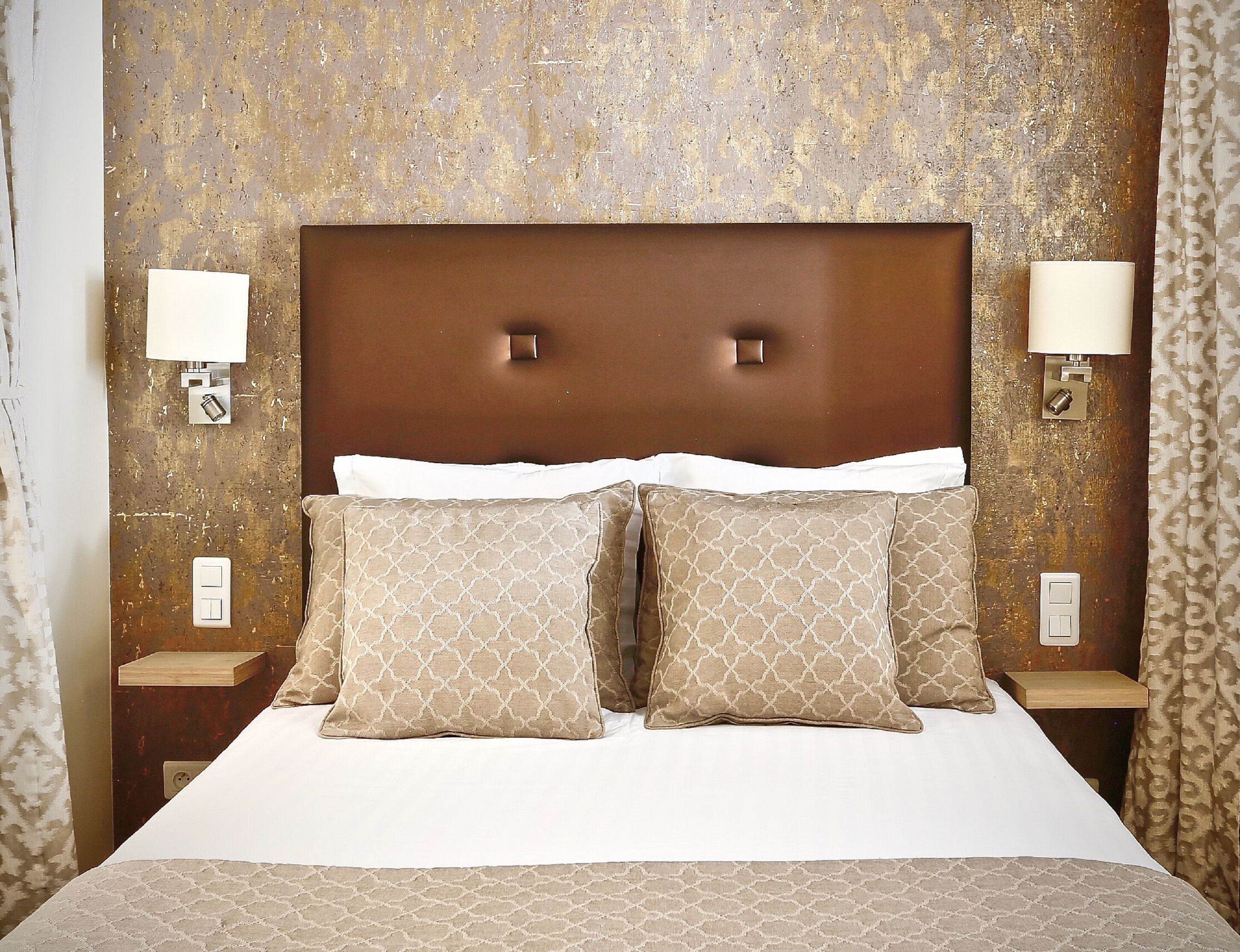 Quarto de hotel com uma cama grande, duas mesas de cabeceira e parede com padrão.