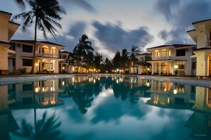 Resort com uma grande piscina, palmeiras e edifícios bem iluminados.