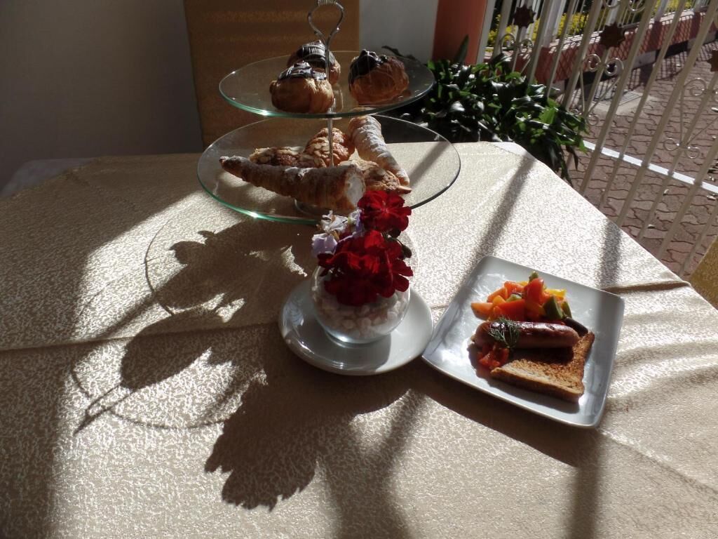 Uma mesa com um expositor de vidro exibindo doces e um prato com sanduíche e vegetais.