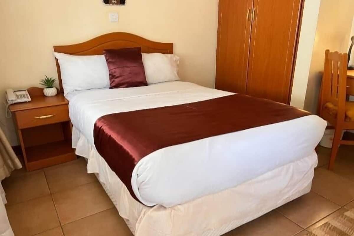 Quarto de hotel padrão com uma cama, mesa de cabeceira com telefone, guarda-roupa e uma cadeira.