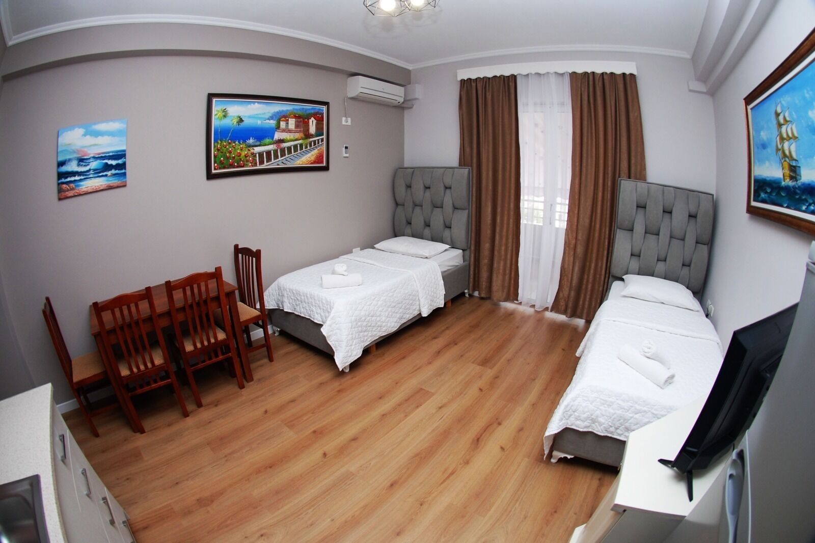 Quarto de hotel com duas camas, uma mesa de jantar com cadeiras e obras de arte nas paredes.