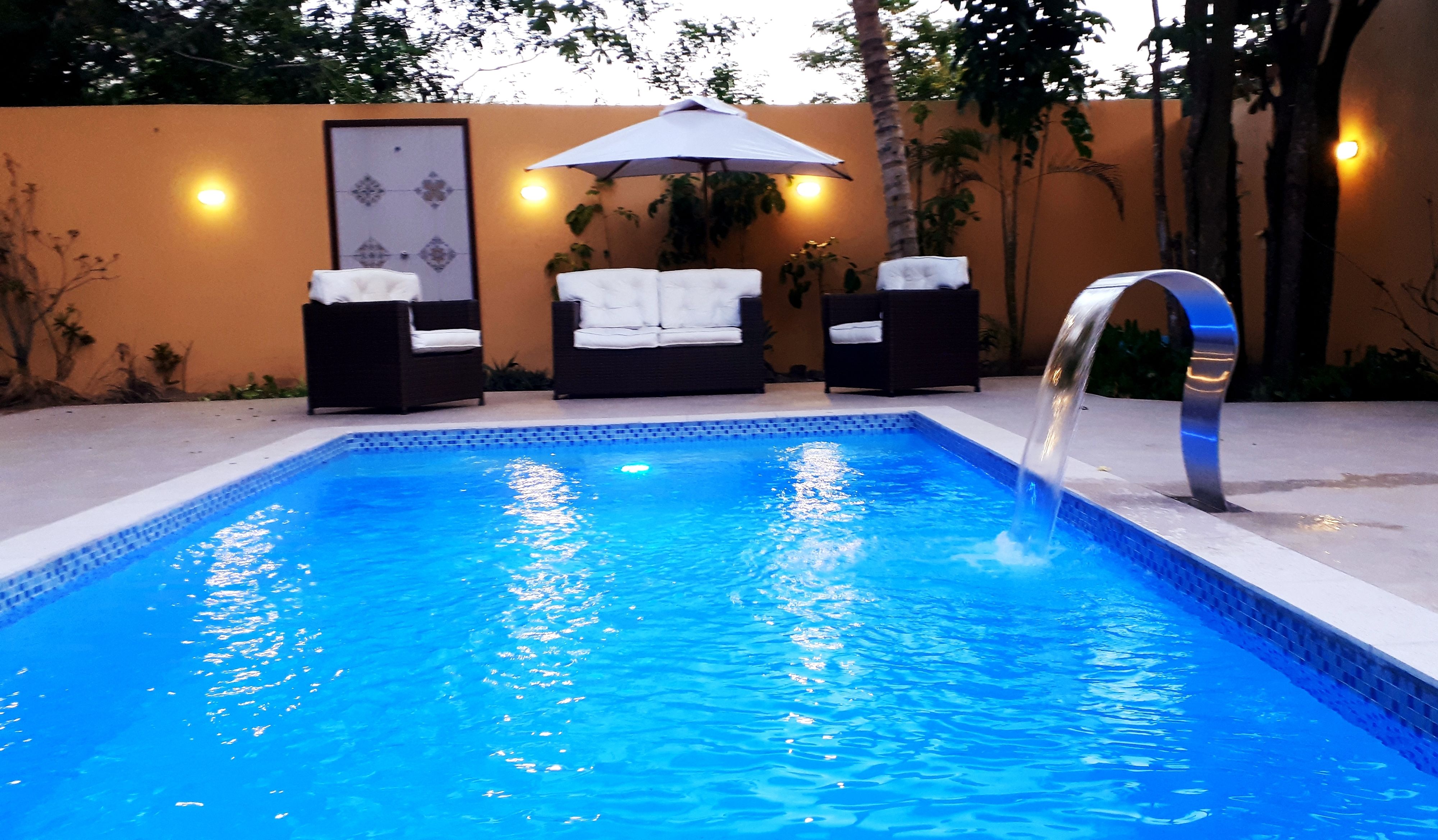 Uma piscina com água cristalina azul, rodeada por espreguiçadeiras e um guarda-sol.