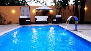 Uma piscina com água cristalina azul, rodeada por espreguiçadeiras e um guarda-sol.