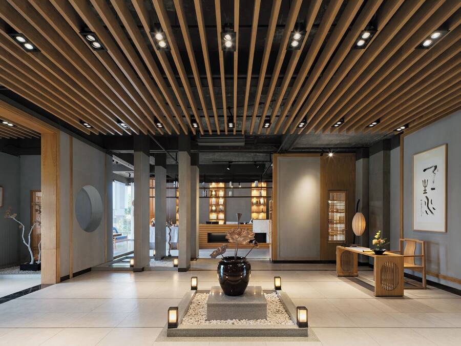 Interior moderno com teto de madeira, um vaso preto no centro e um balcão de recepção com bancos de madeira.