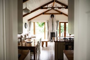 Uma cozinha acolhedora com uma mesa de madeira, cadeiras, fogão e uma janela grande com cortinas.