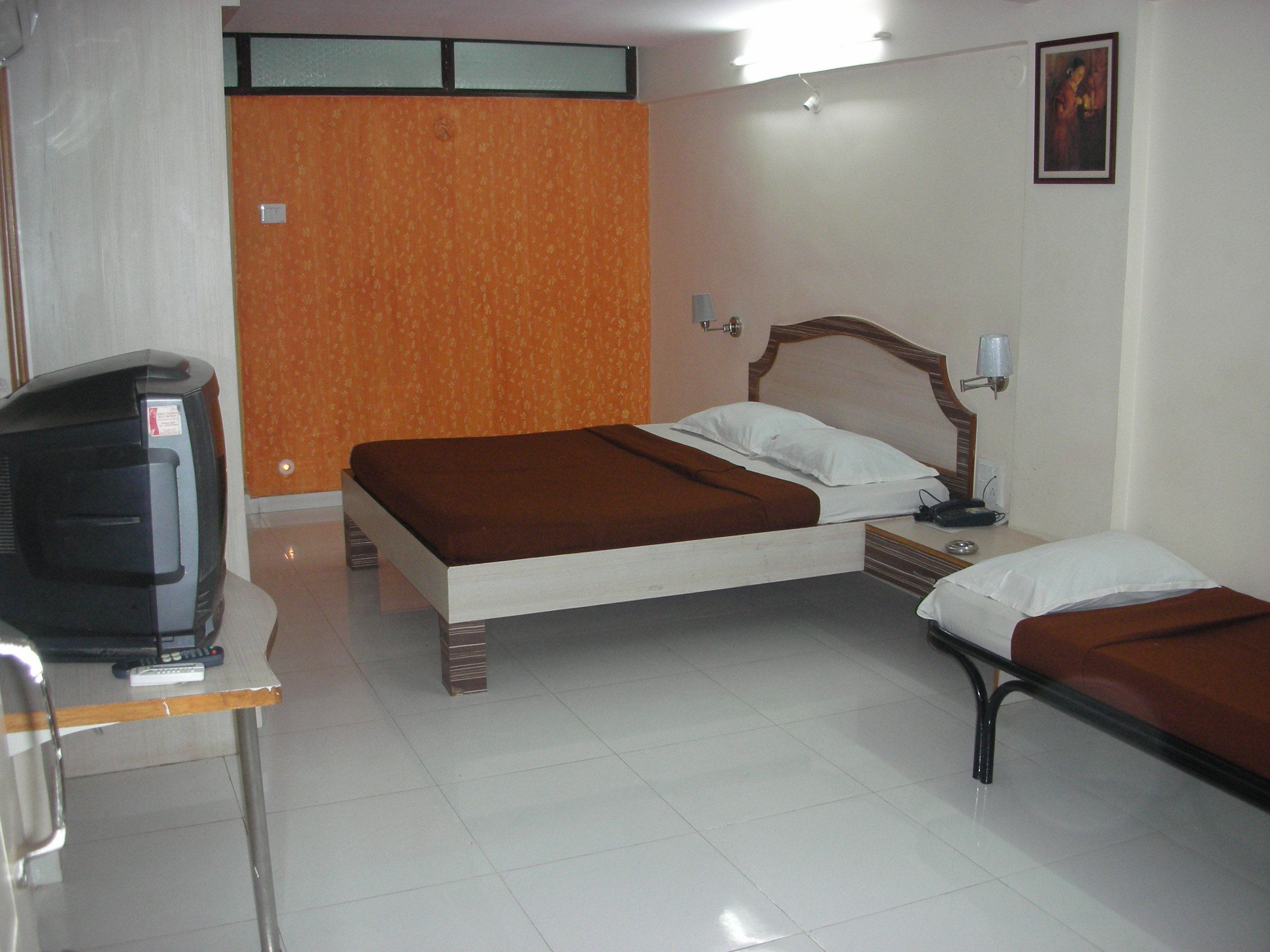 Quarto de hotel com cama, escrivaninha e televisão, e mesa de cabeceira.