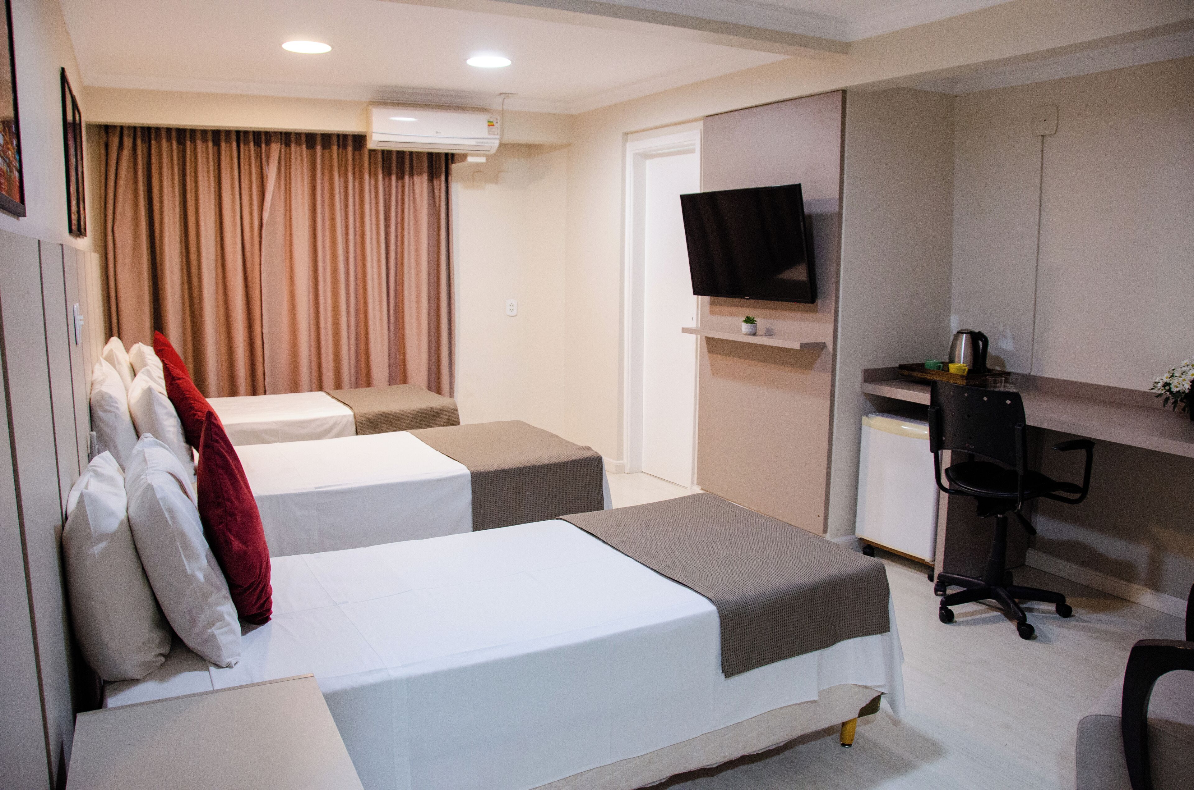 Quarto de hotel com duas camas, uma escrivaninha, uma cadeira, uma televisão e ar condicionado.