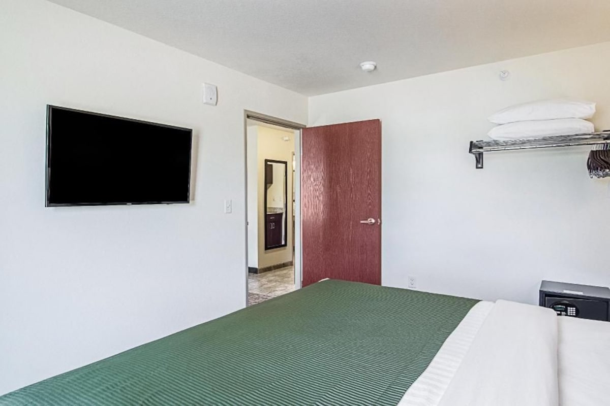 Quarto de hotel com cama, televisão, porta e cabideiro.