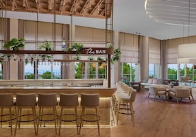 Uma área de bar com balcão, banquetas e uma placa com a inscrição 'The BAR'.