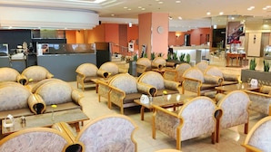 Um hall de hotel espaçoso, com várias áreas de estar, balcão de recepção e escadaria para um andar superior.