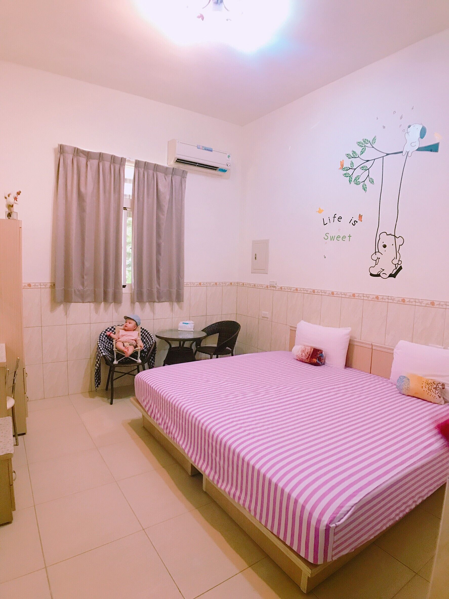 Quarto com cama, uma mesa pequena, uma cadeira e janela com cortinas.