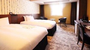Quarto de hotel com duas camas, uma escrivaninha, uma cadeira e uma mesinha.