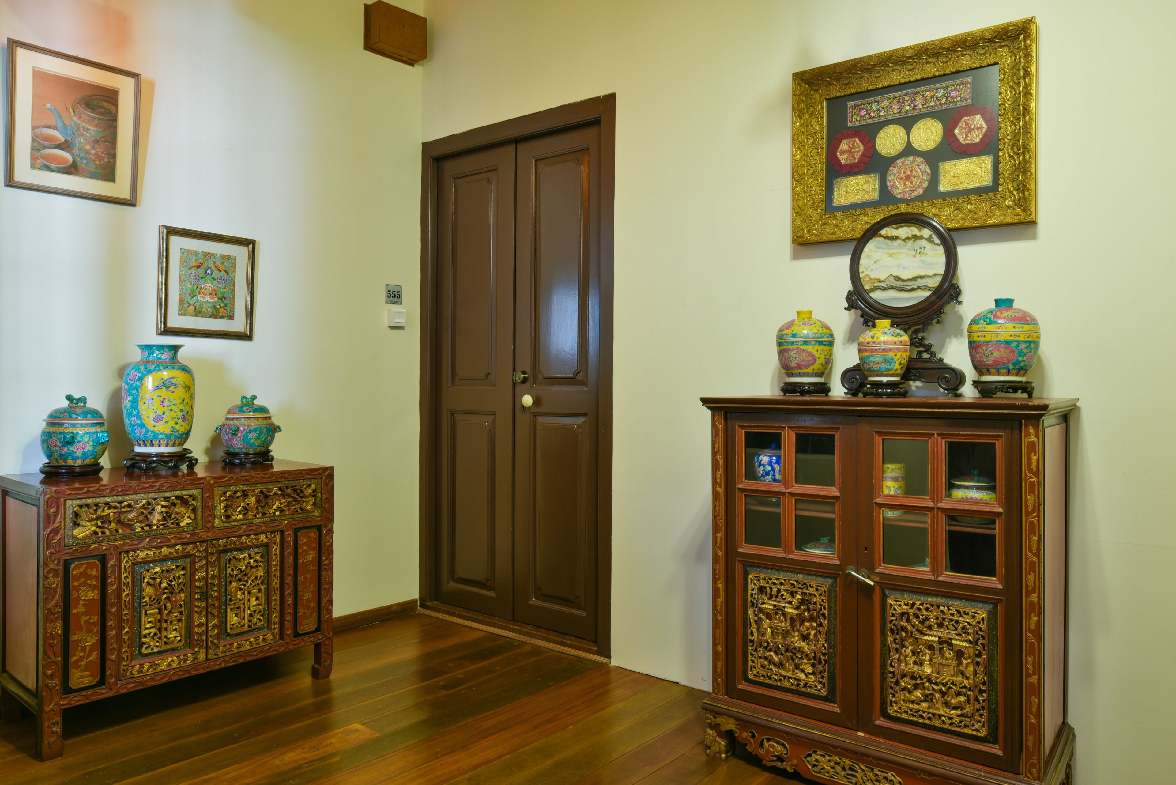 Um corredor com porta de madeira, um armário com vasos decorativos e obras de arte emolduradas nas paredes.